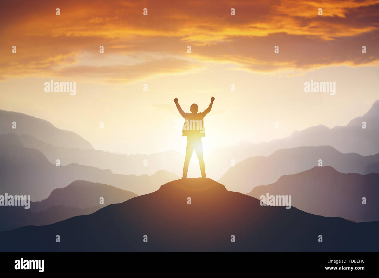 Man standing on edge of mountain feeling victorious with arms up in the ...