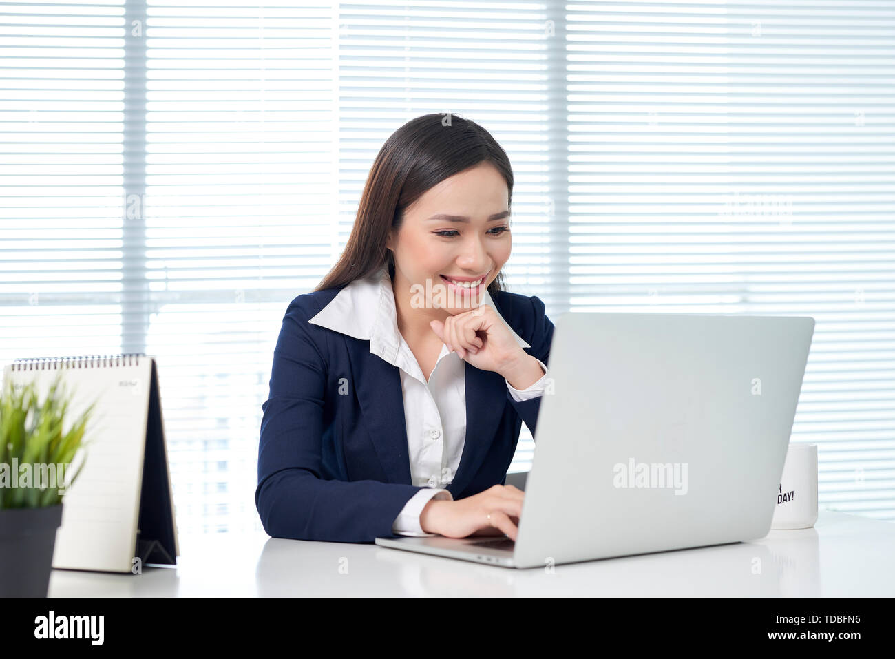 Cheerful employee is holding glasses and looking at screen of laptop ...
