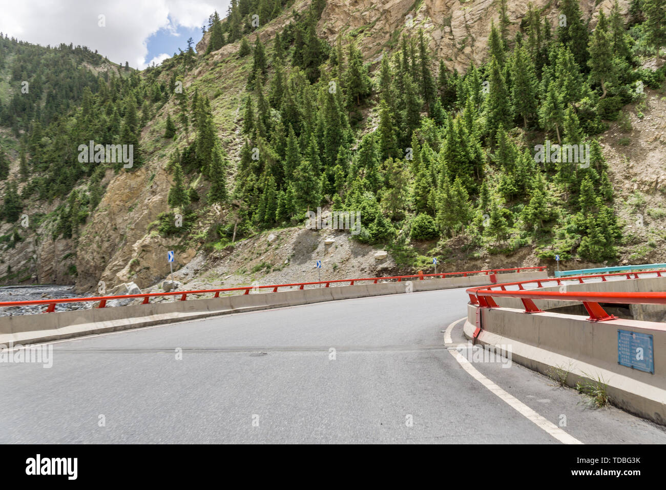 G217 Duku Highway bend in alpine forest under summer blue sky and white ...