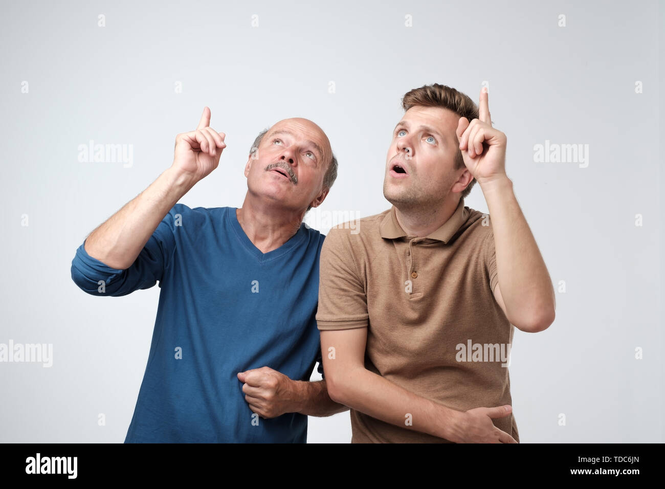 Two men father and son looking upwards, pointing index fingers up with ...