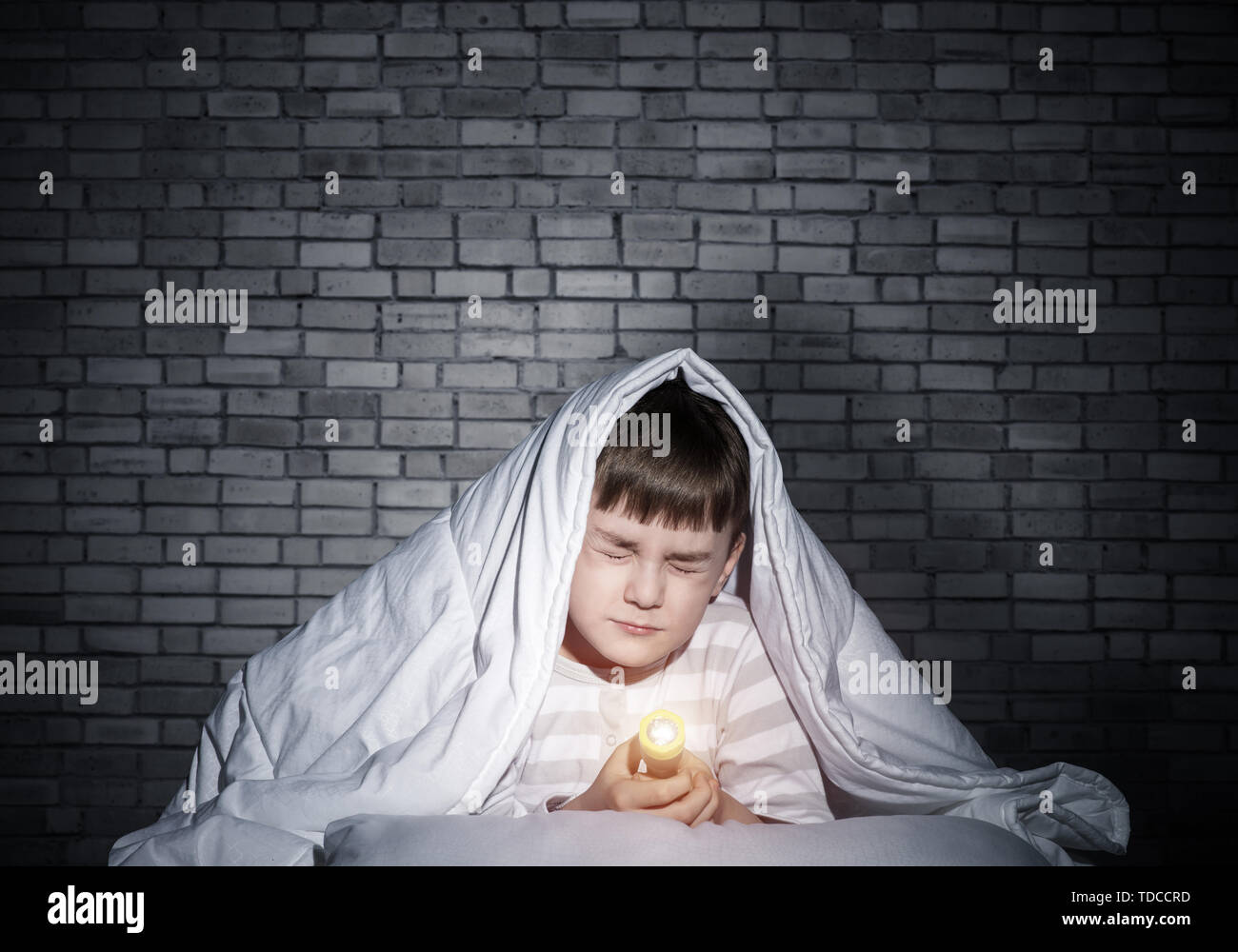 Frightened child with flashlight hiding under blanket. Scared kid with ...