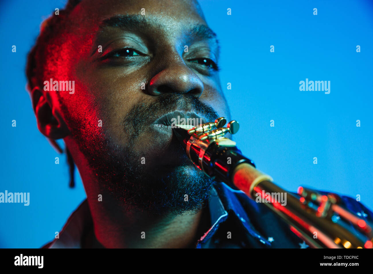 Young african-american jazz musician playing the saxophone on blue ...