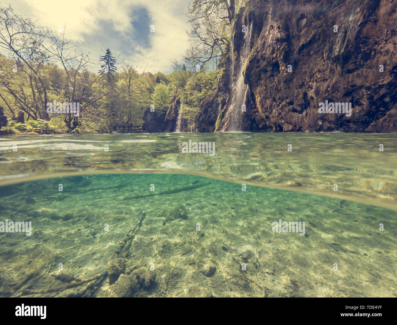 Amazing split view of lake with sunken tree trunk and waterfall in the ...