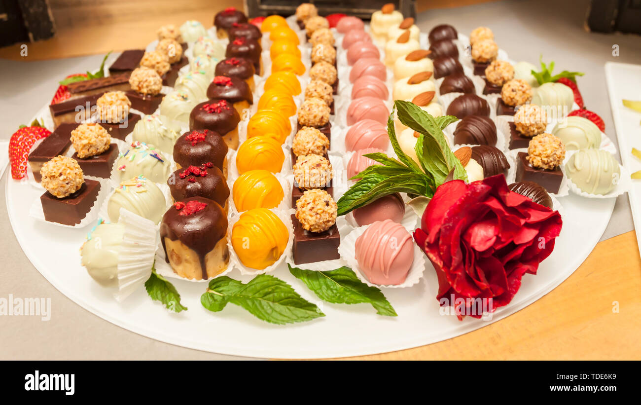 Small assorted cakes lined up decorated on dessert buffet with red rose ...