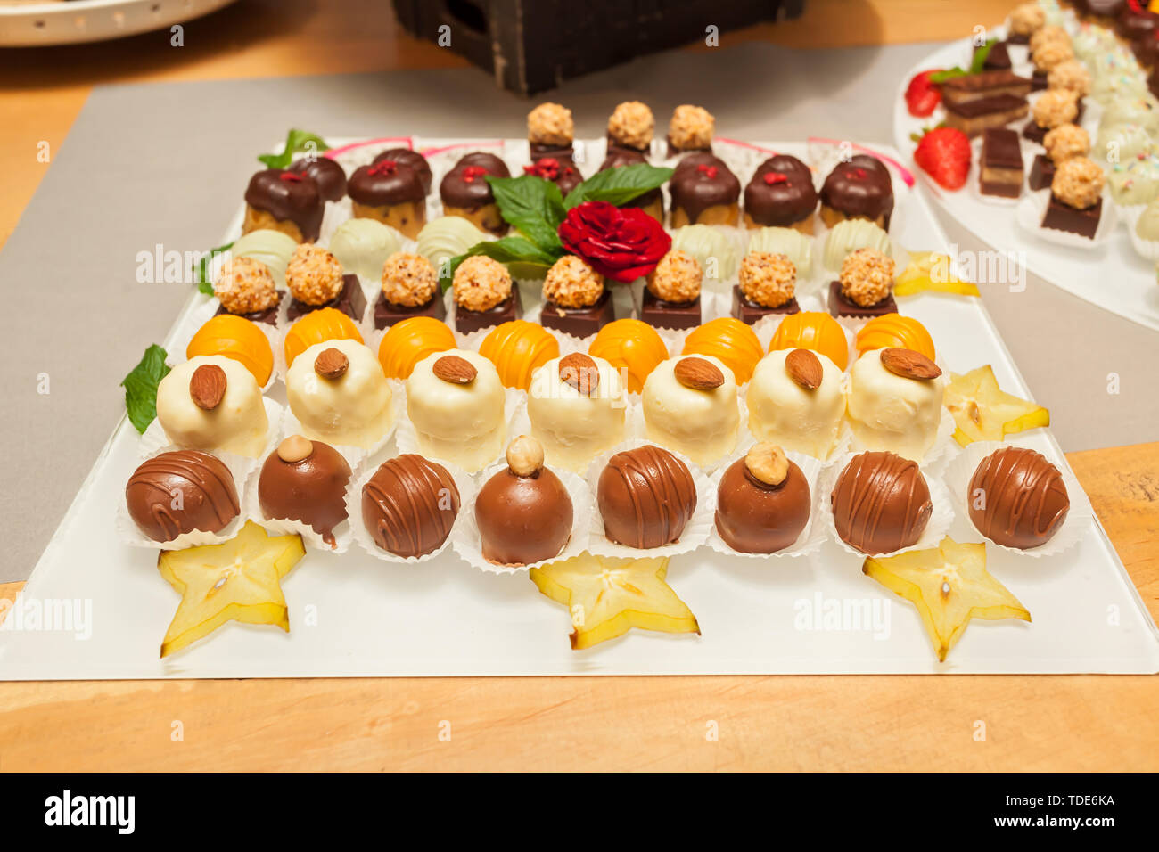 Small assorted cakes lined up decorated on dessert buffet with red rose ...