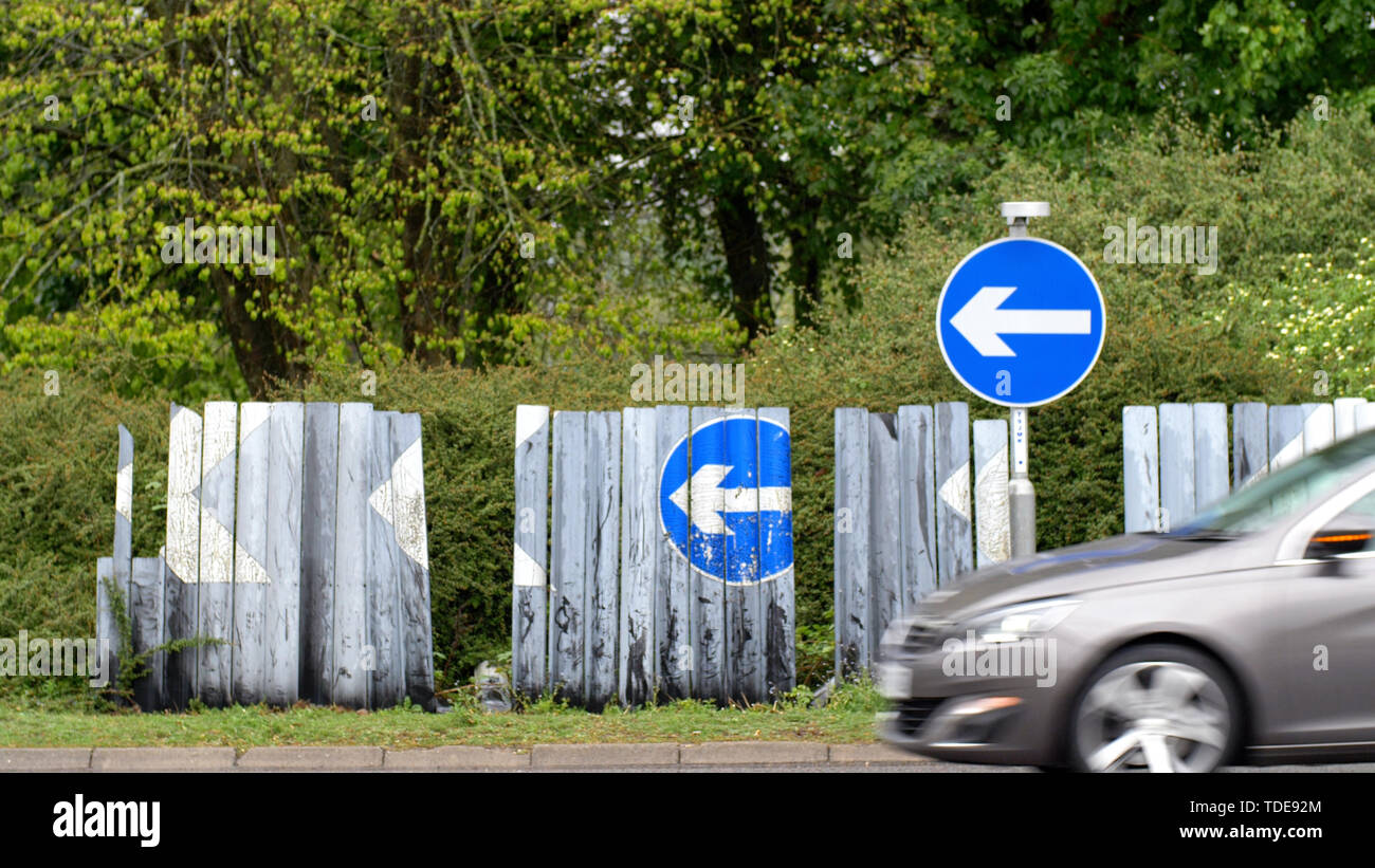 Blue road traffic direction arrow signs on british roundabout on rainy ...