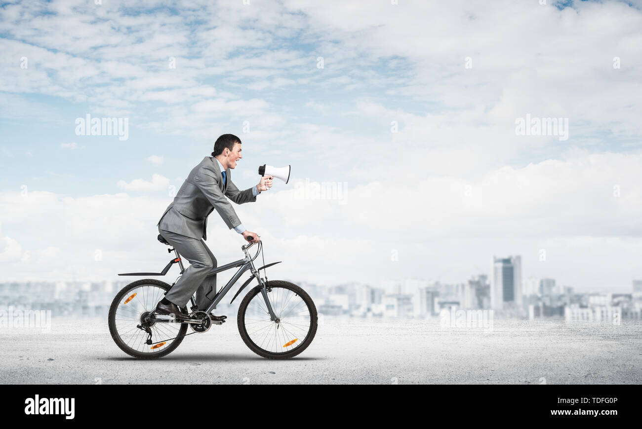 Businessman with megaphone on bike at sunny day. Marketing and ...