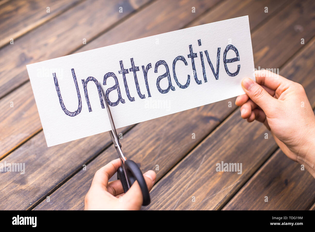 woman cuts white paper with word unattractive on table Stock Photo - Alamy