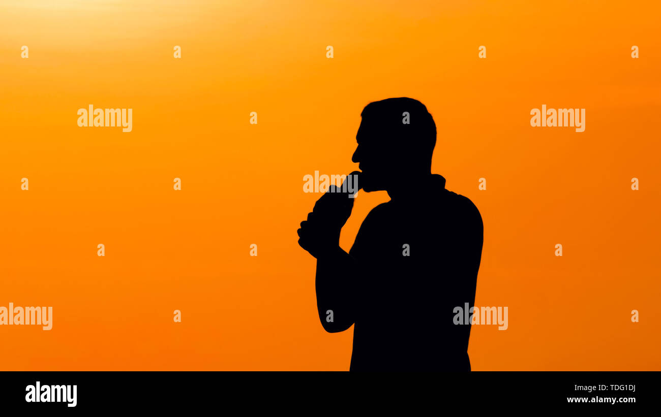 Unrecognizable man silhouette speaking into microphone on city street ...