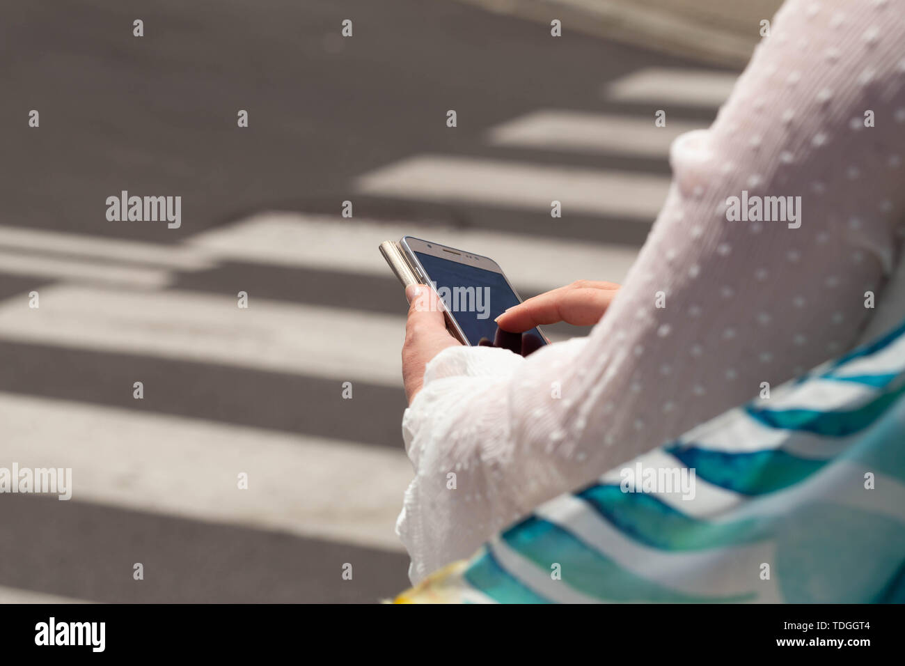 A woaman at a pedestrian crossing looking at the smartphone / safety ...