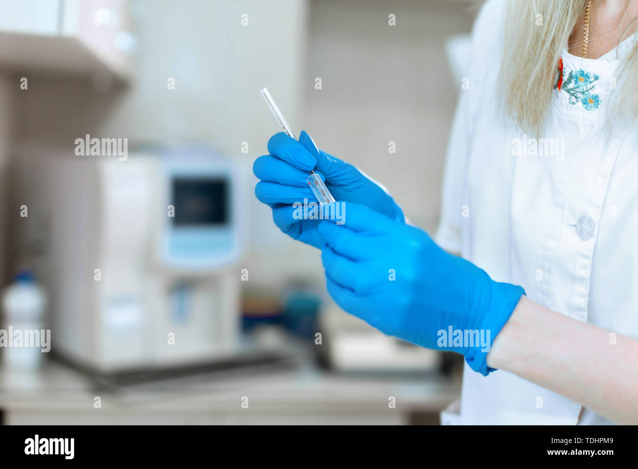 A female blonde lab technician takes a blood sample with blue gloves ...