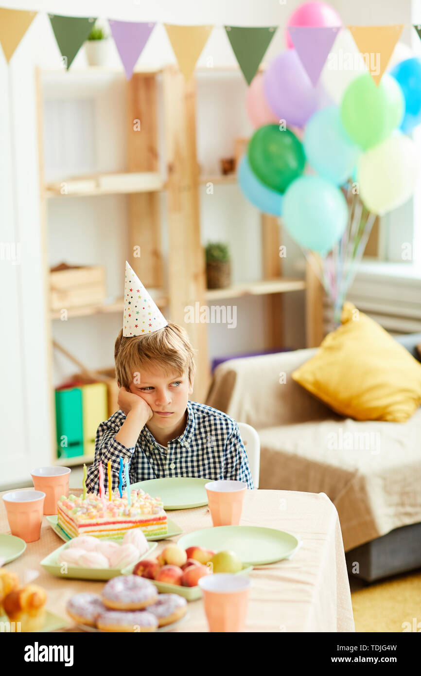 Portrait of sad boy sitting at table alone during Birthday party, copy ...