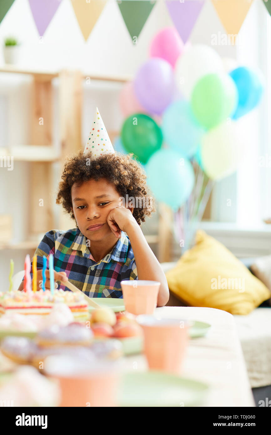 Portrait of sad African-American boy sitting at table alone during ...