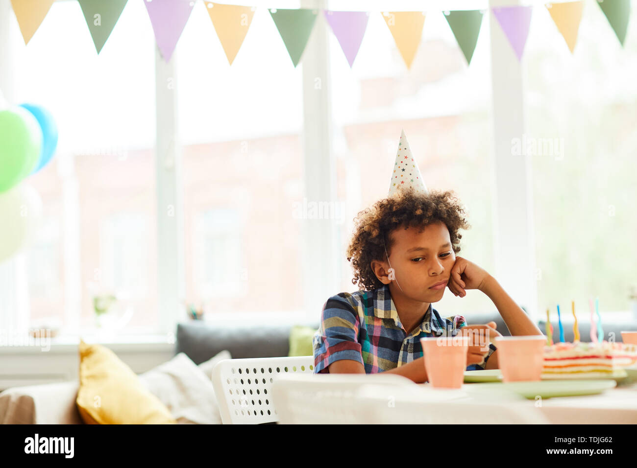 Portrait of sad African-American boy sitting alone at Birthday party ...