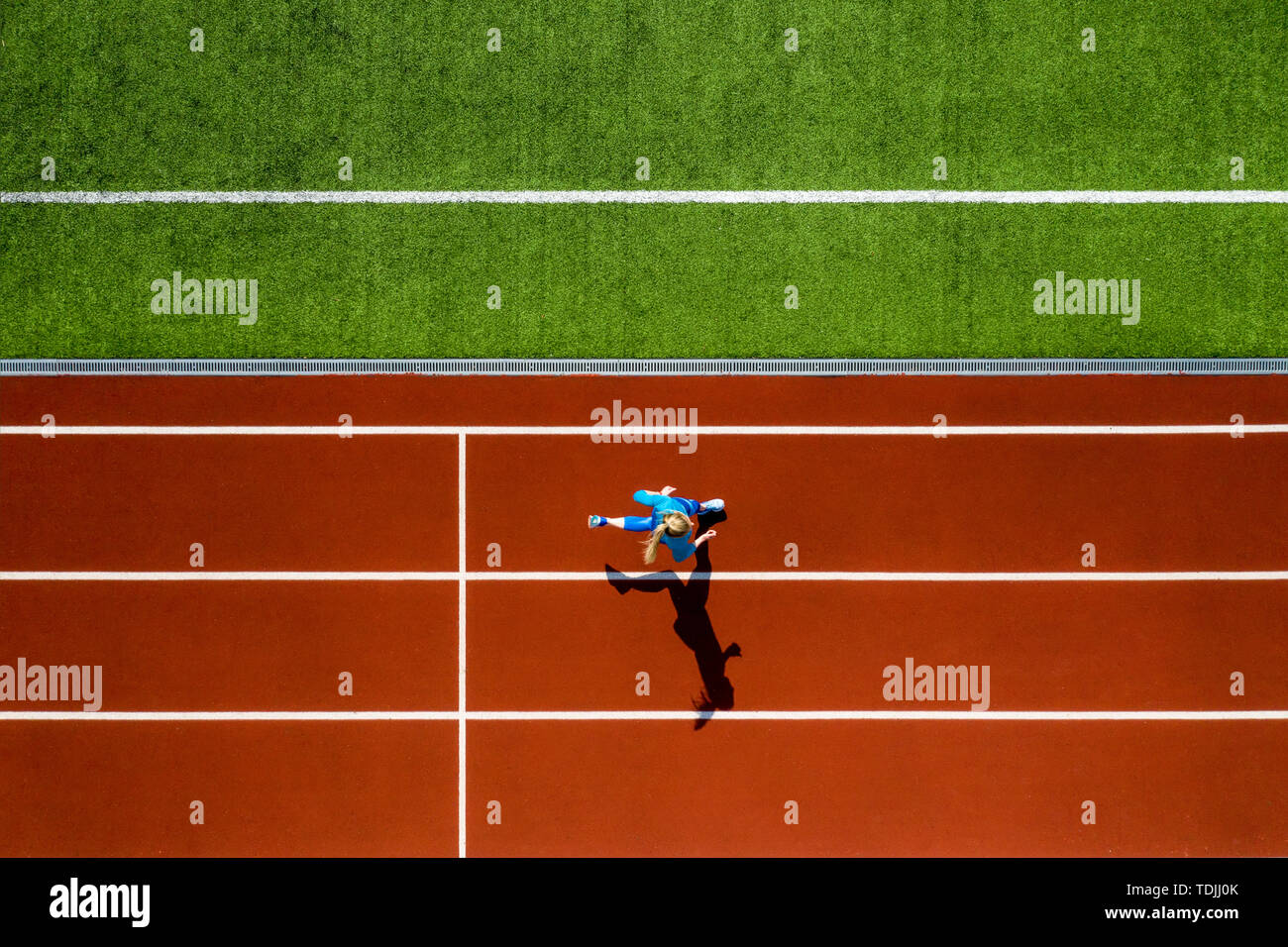 Blonde girl in a blue sportswear and sneakers runs on the running track ...