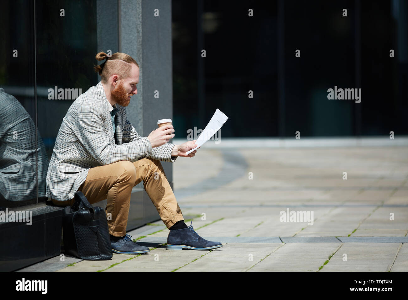 Thoughtful handsome young freelance analyst sitting outdoors and ...