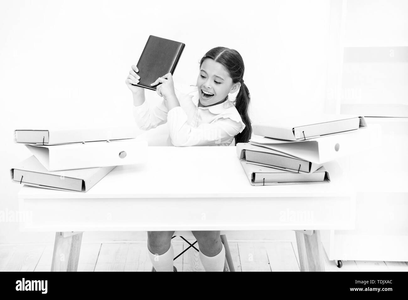 Capricious girl. Small girl raising book at folders. Angry girl hates ...