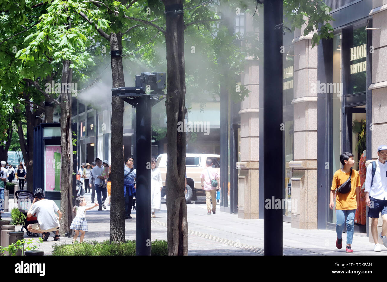 Tokyo, Japan. 16th June, 2019. People stroll under water mist sprayers ...