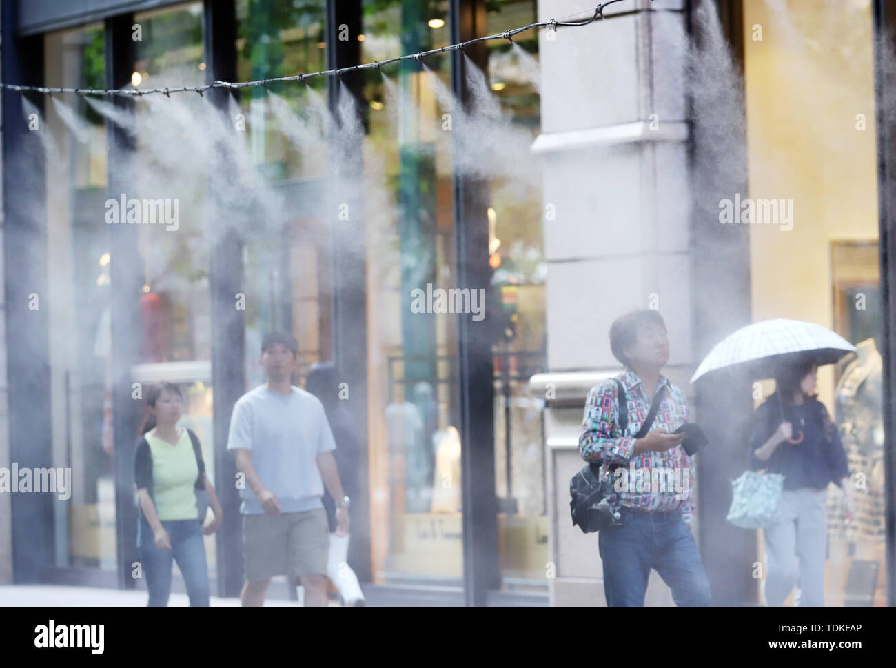 Tokyo, Japan. 16th June, 2019. People stroll under water mist sprayers ...