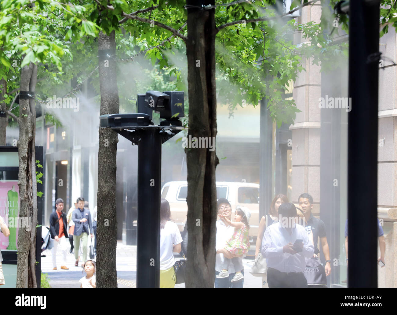 Tokyo, Japan. 16th June, 2019. People stroll under water mist sprayers ...