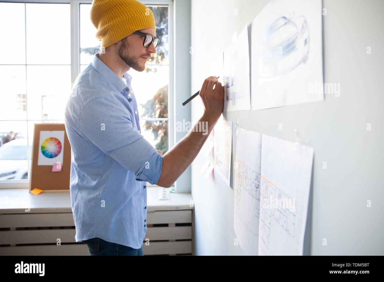 Young creative man writing down ideas on wall full of sticky notes ...
