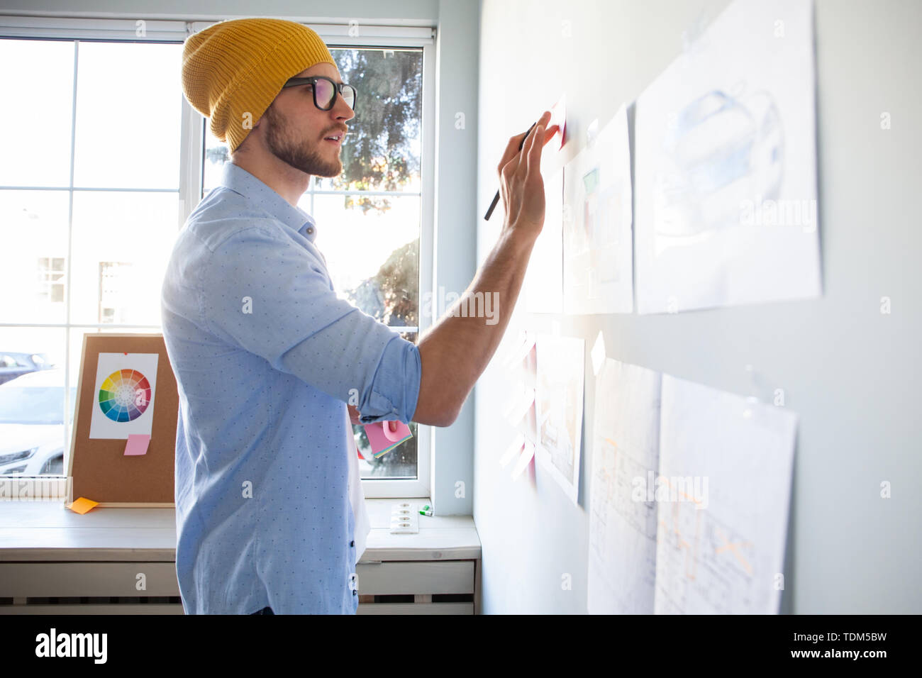 Young creative man writing down ideas on wall full of sticky notes ...