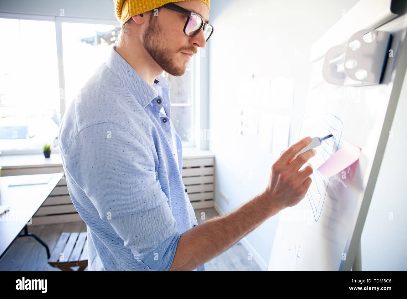 Young creative man writing down ideas on wall full of sticky notes ...