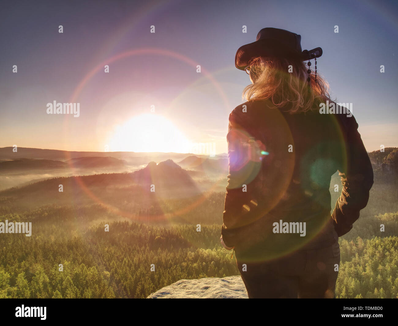 Cheering young woman traveler hiking on rocky mountain promontory above ...