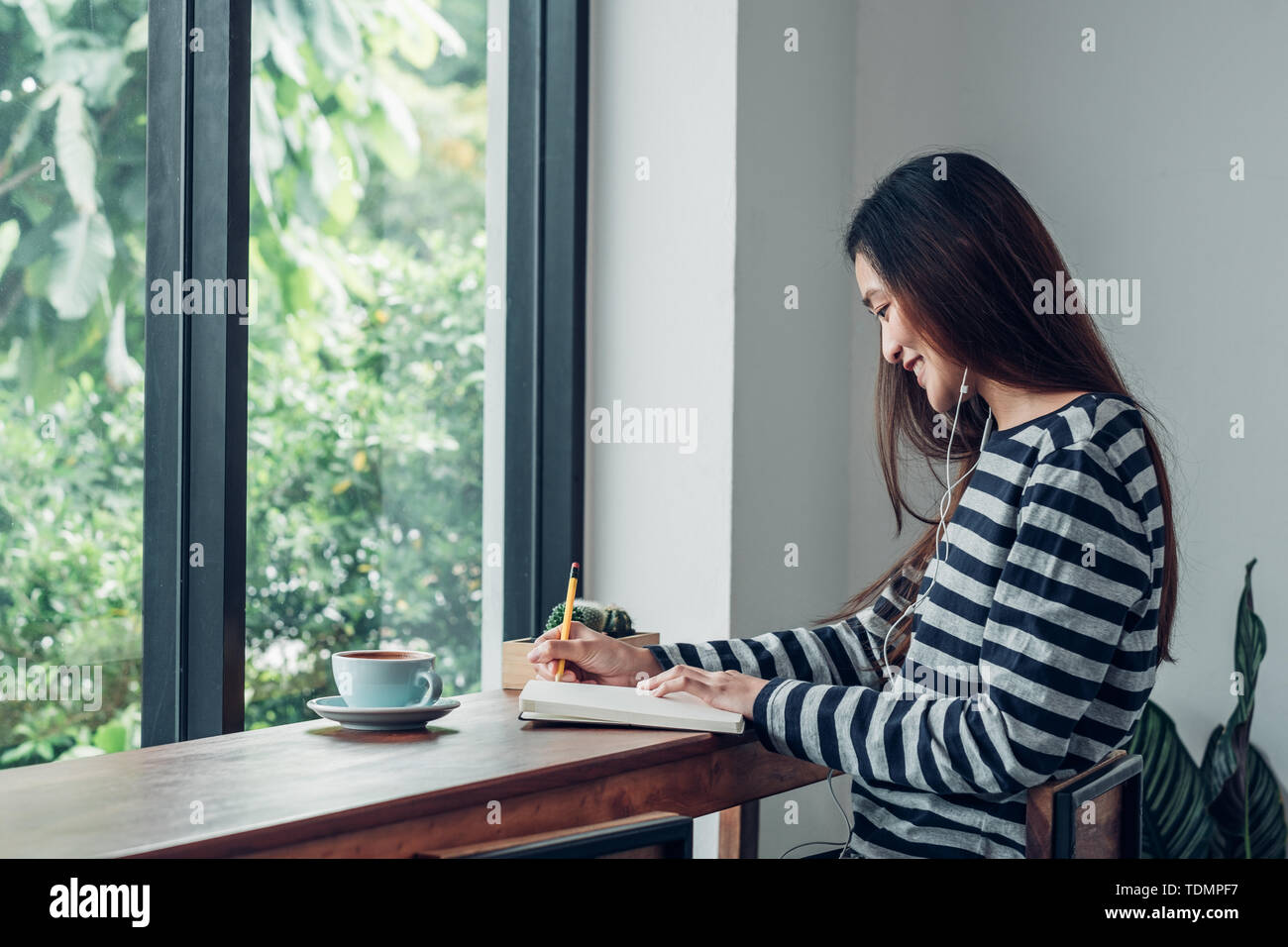 Asian woman writing book listening music with mobile sitting at cafe ...