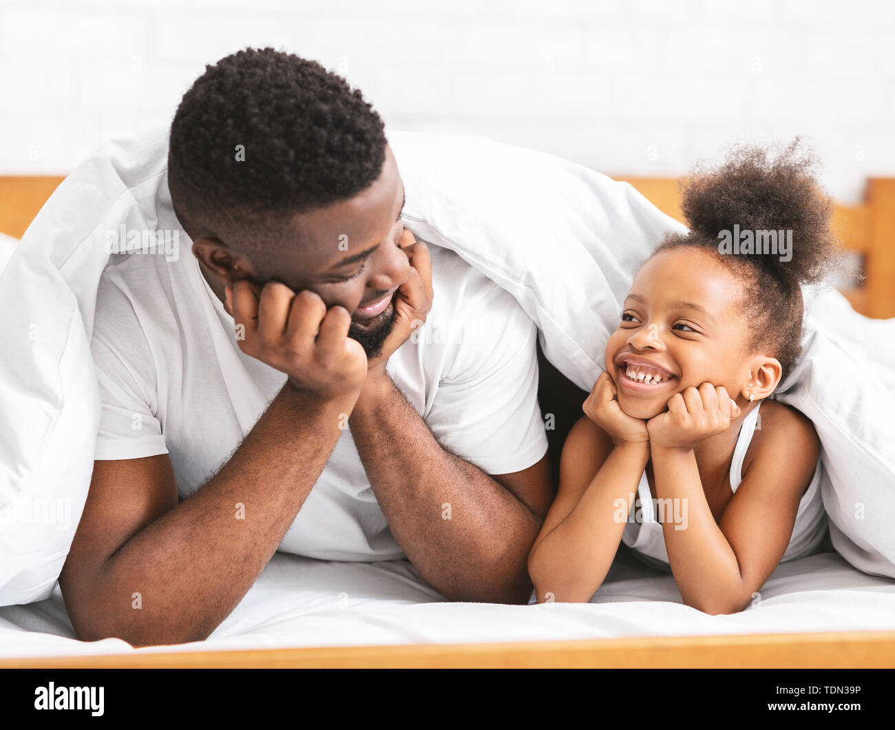 Cute african dad and daughter lying on bed and smiling to each other ...