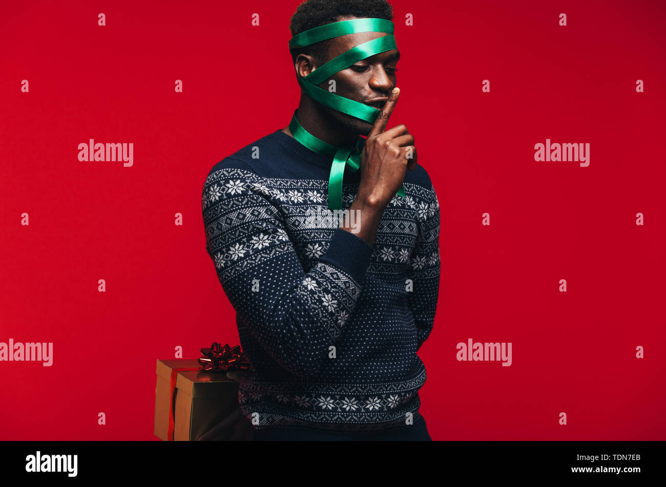 African guy wrapped in a ribbon holding a gift box and gesturing ...