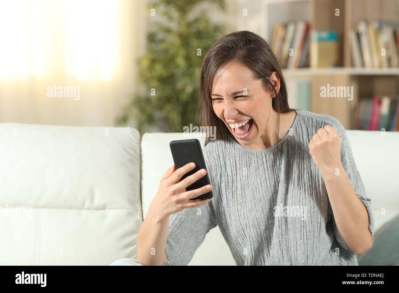 Excited woman checking smart phone sitting on a couch in the living ...