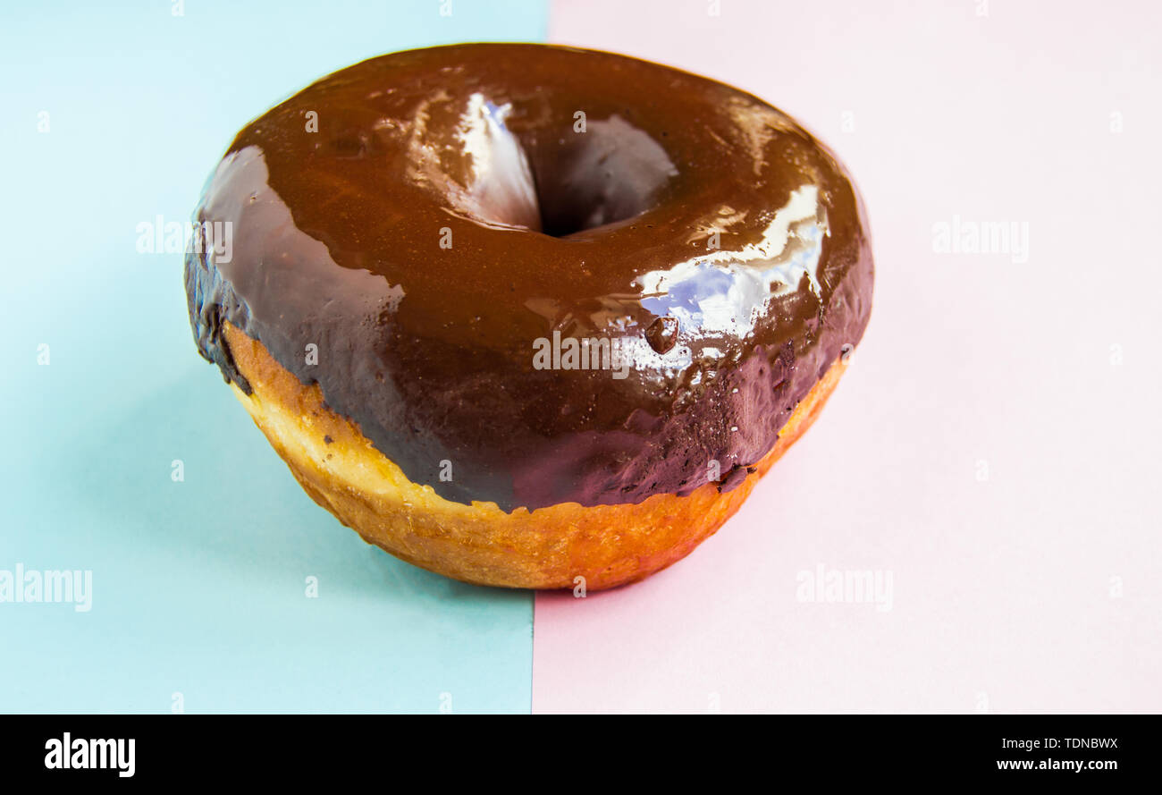 Delicious donut with shiny chocolate icing on pastel pink-blue ...