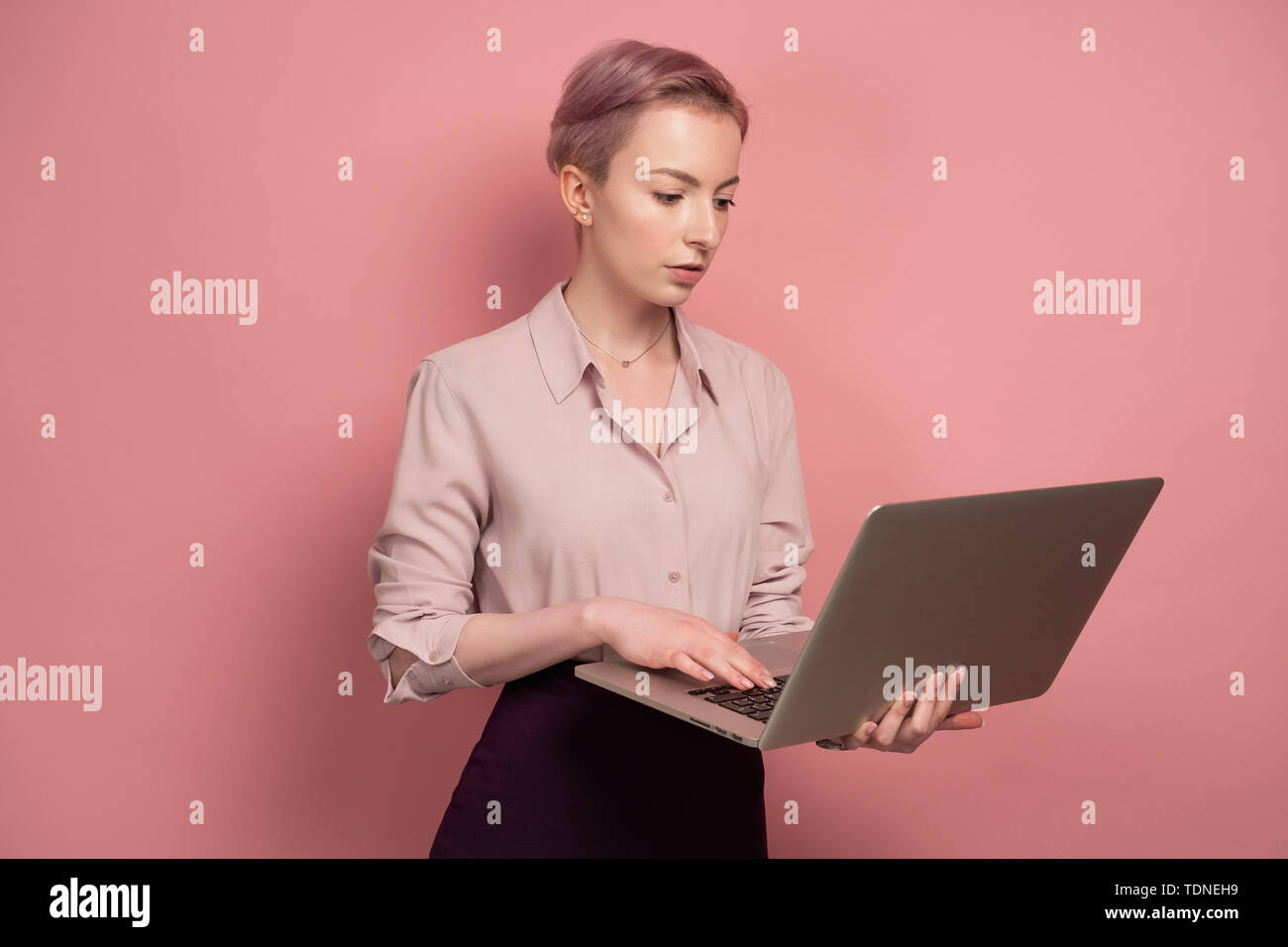 Pink-haired young businesswoman works with her laptop posing over pink ...