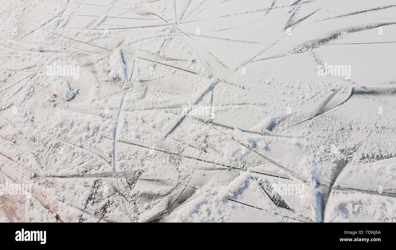 Winter background of frozen ground with ice, with traces of skates that ...