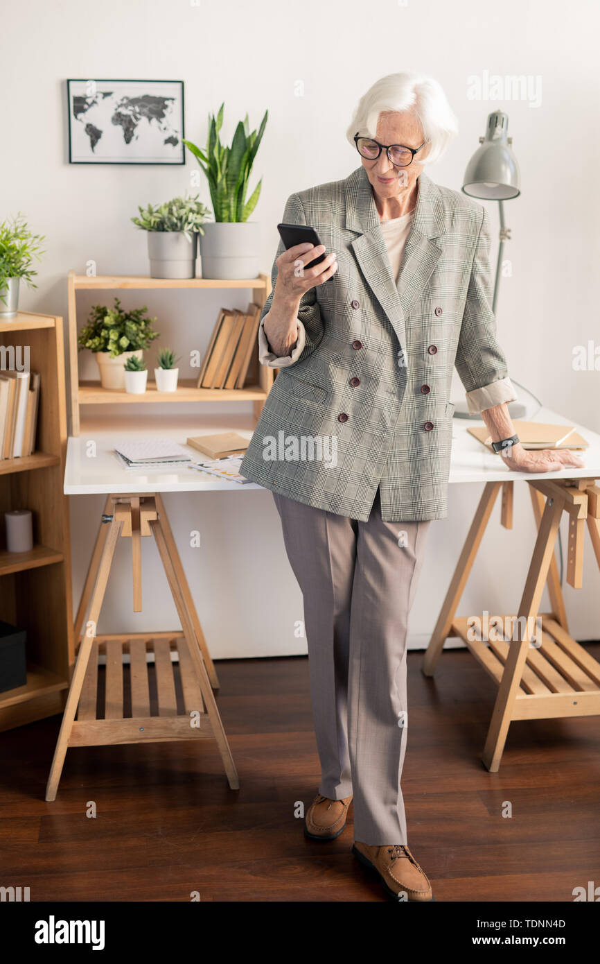 Elegant retired white-haired woman in grey suit texting in smartphone ...