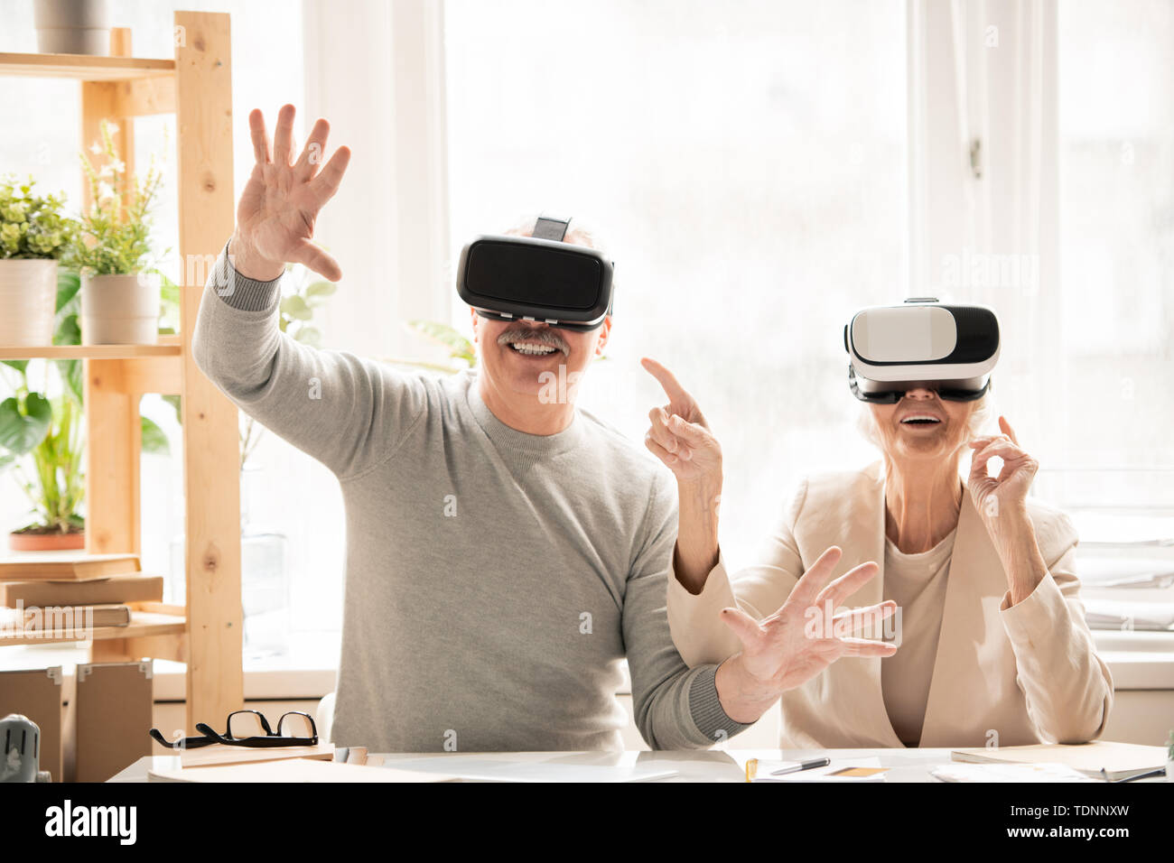 Happy senior female in vr goggle pointing at her husband in headset ...