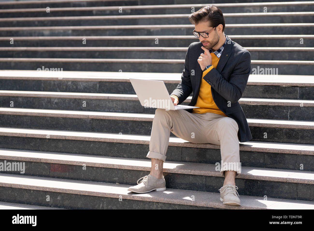 Young creative man in smart casual looking at laptop display while ...