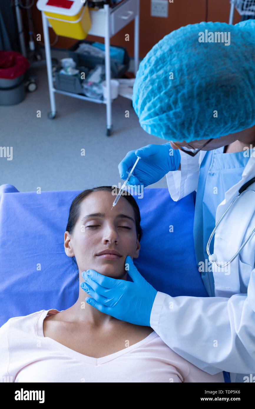 Male surgeon giving injection to face of female patient at hospital ...