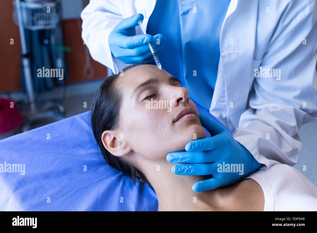 Male surgeon giving injection to face of female patient at hospital ...