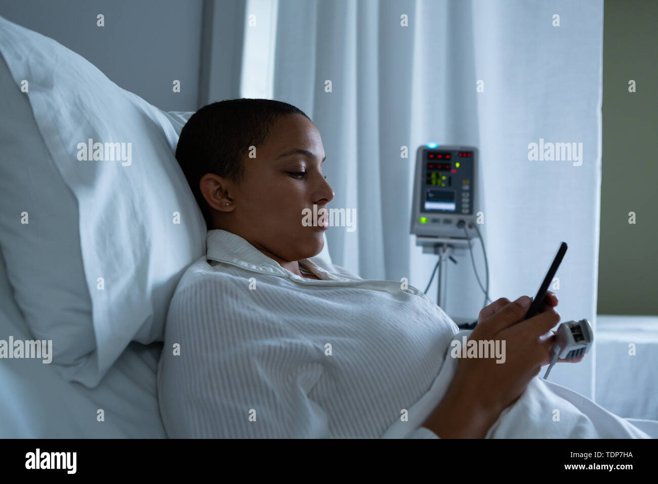 Female patient using mobile phone while lying on bed Stock Photo - Alamy