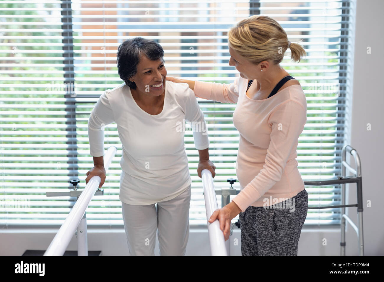 Female physiotherapist helping patient walk with parallel bars Stock ...