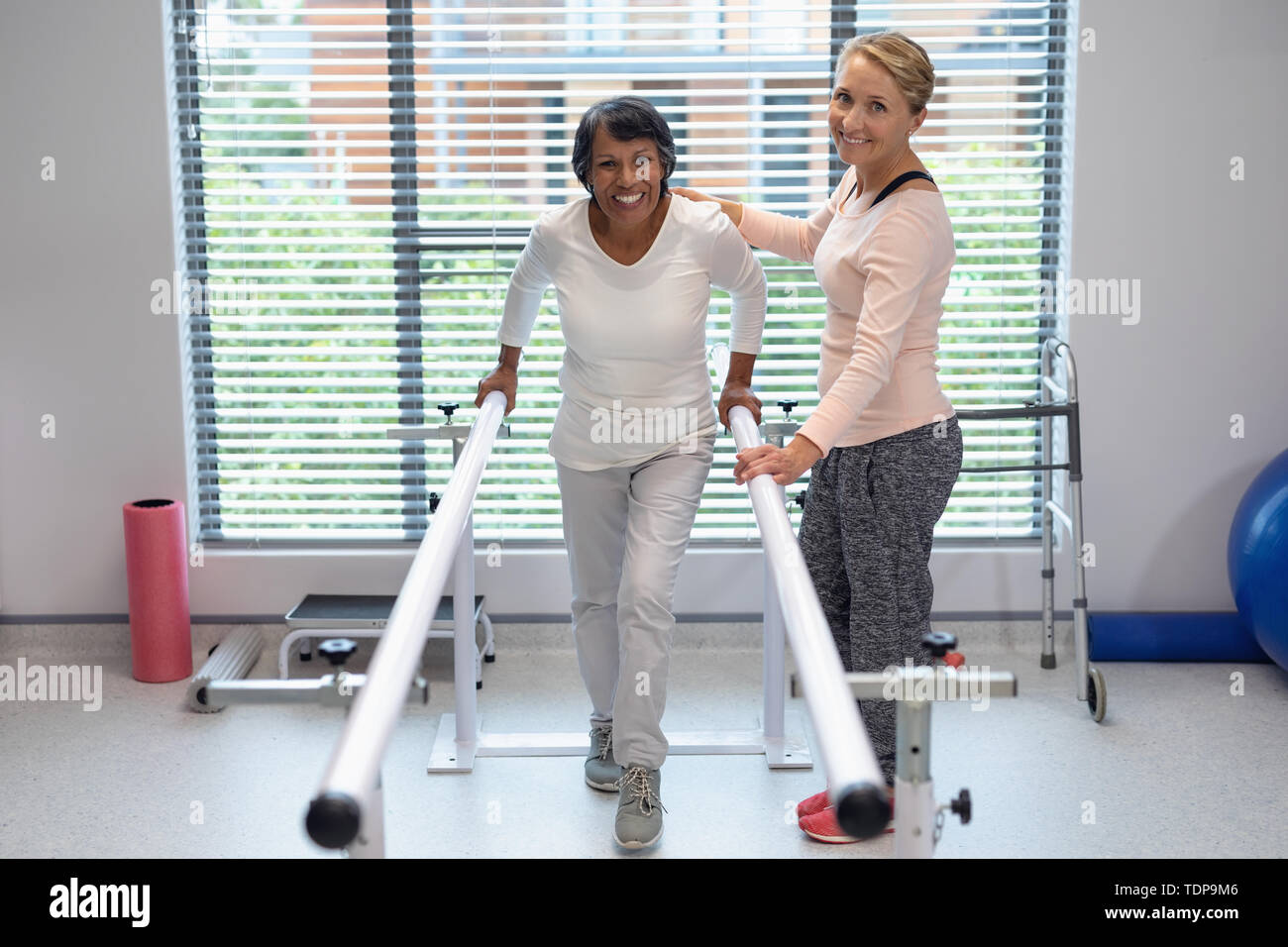 Female physiotherapist helping patient walk with parallel bars Stock ...