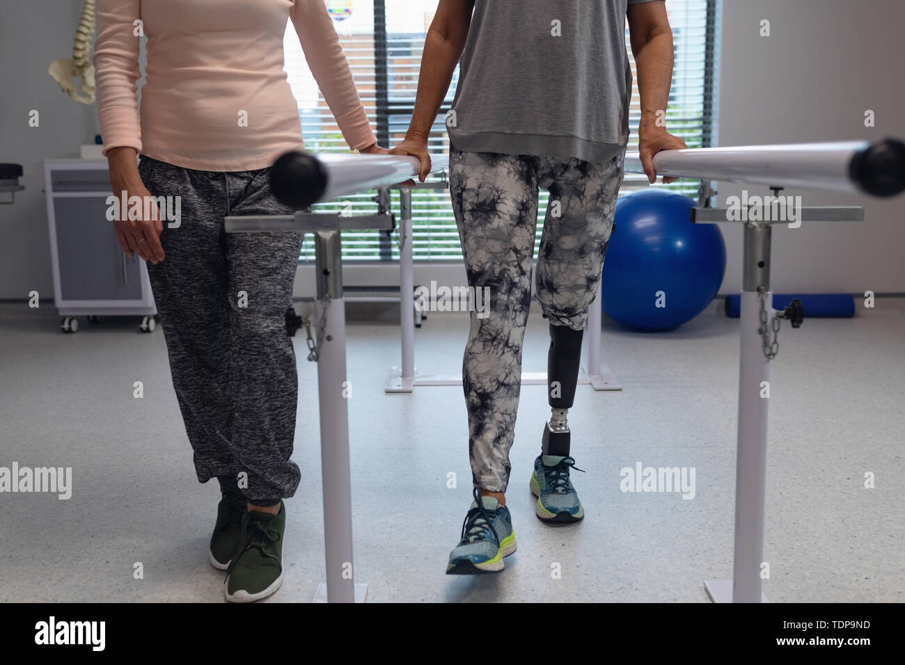 Female physiotherapist helping patient walk with parallel bars in the ...
