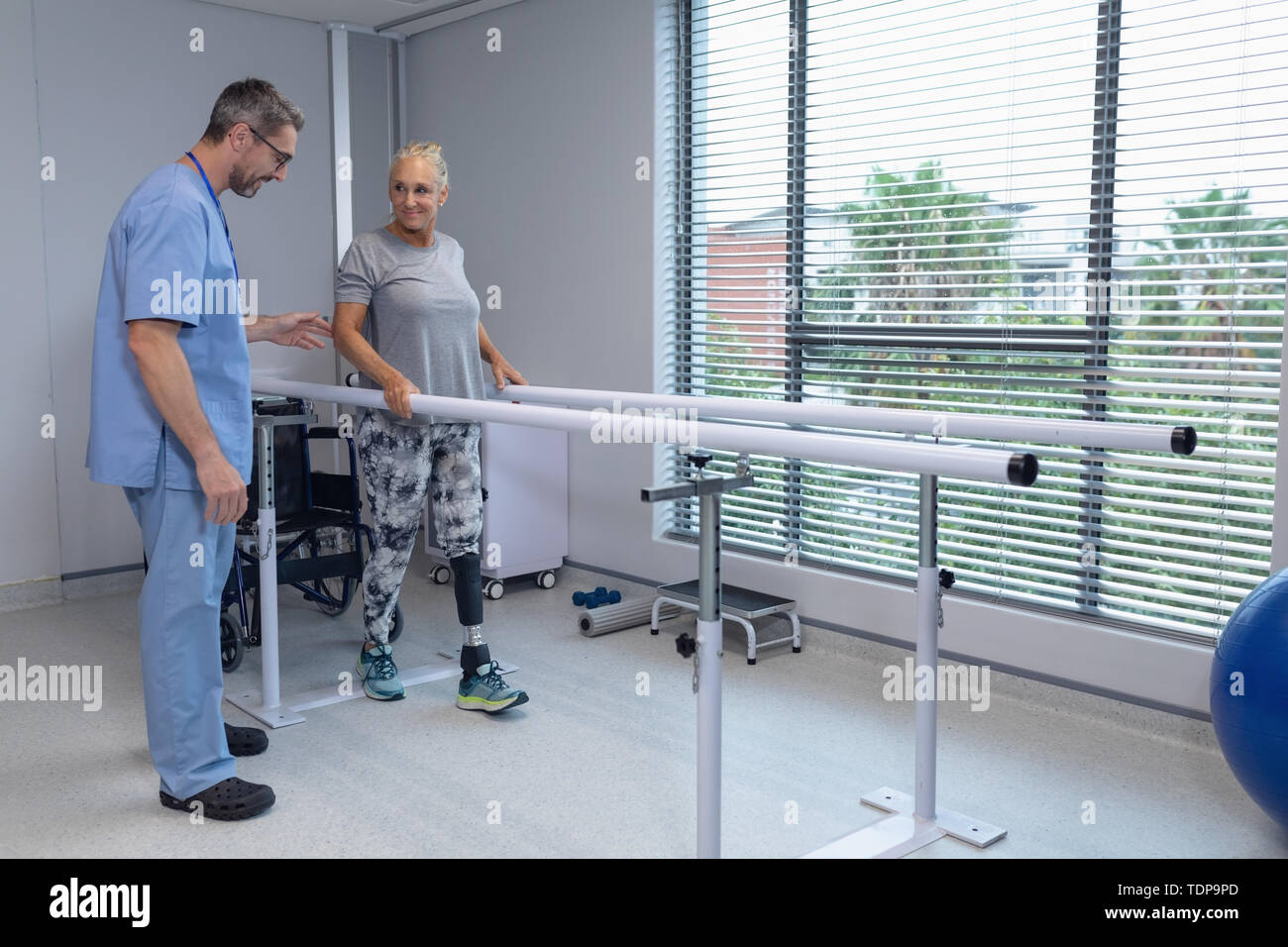 Male physiotherapist helping patient walk with parallel bars Stock ...