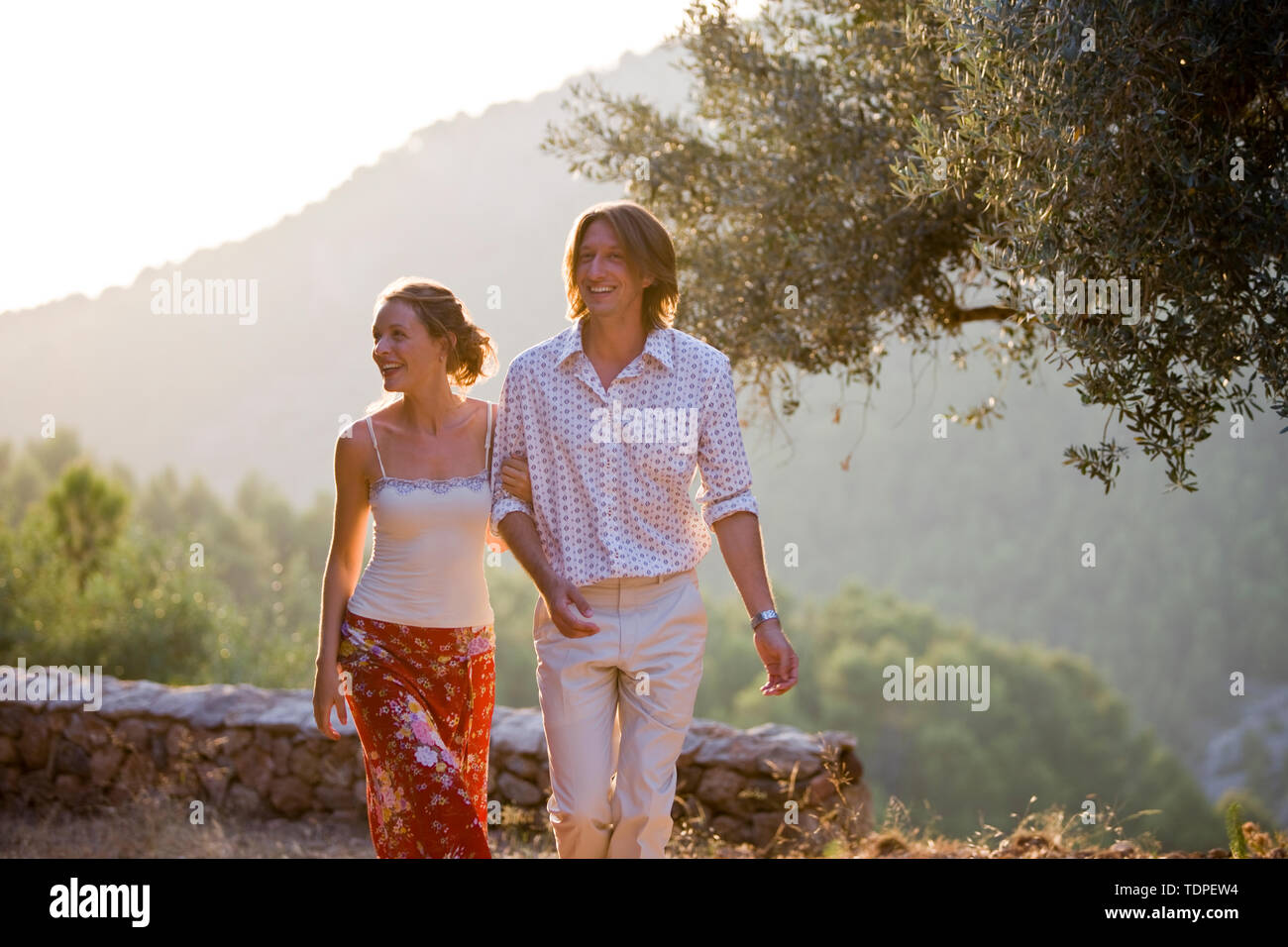Mid adult couple hugging while walking on a country lane at sunset ...