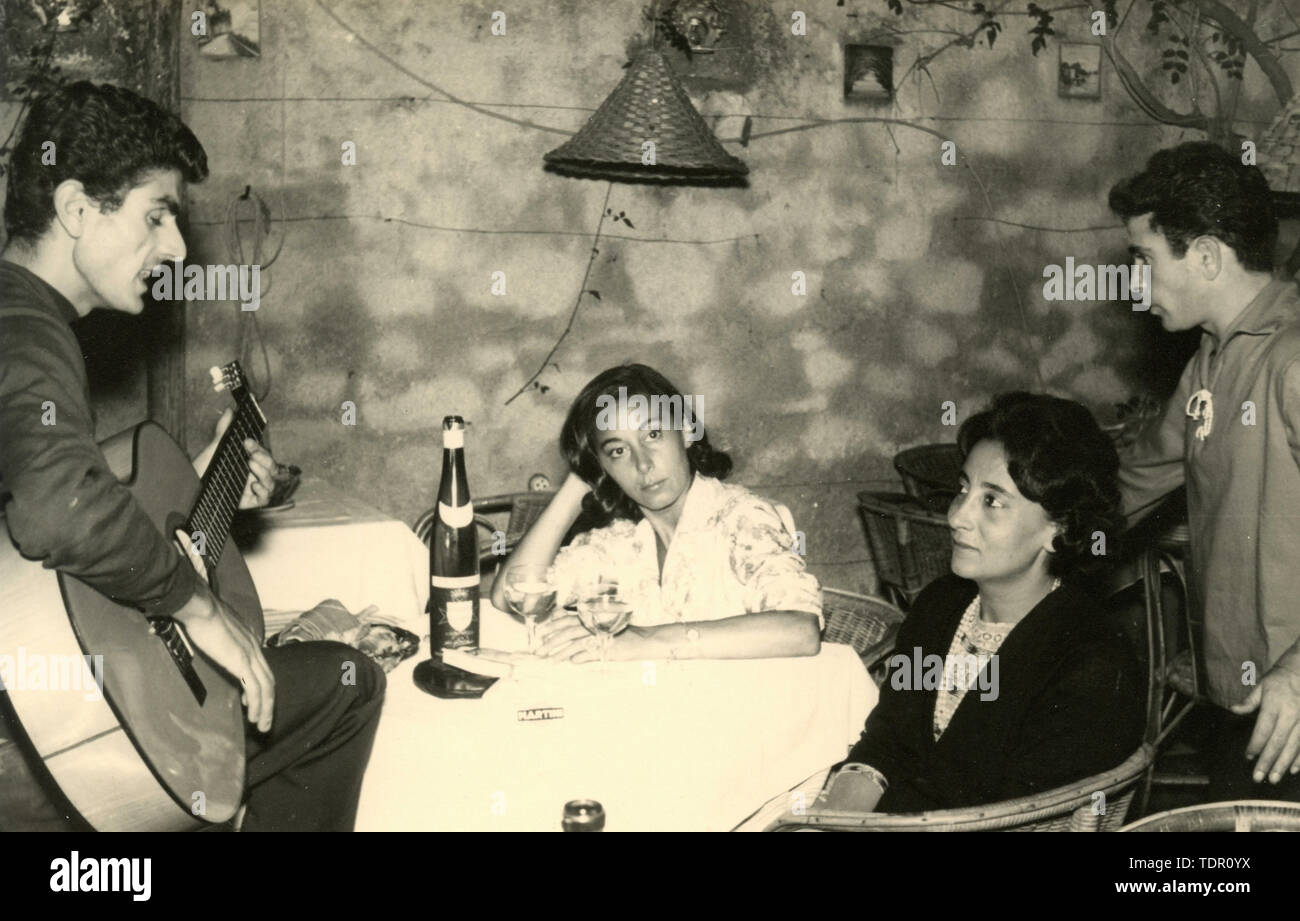 Two women at the restaurant with street singer, Capri, Italy 1960s ...