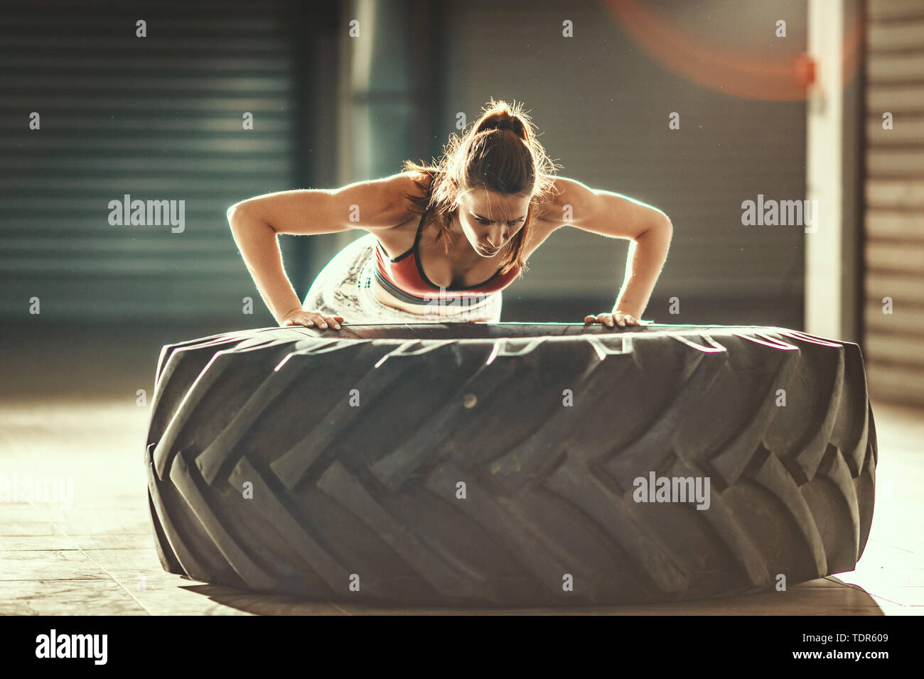 Young muscular woman is doing push-up exercise on a tire at cross fit ...
