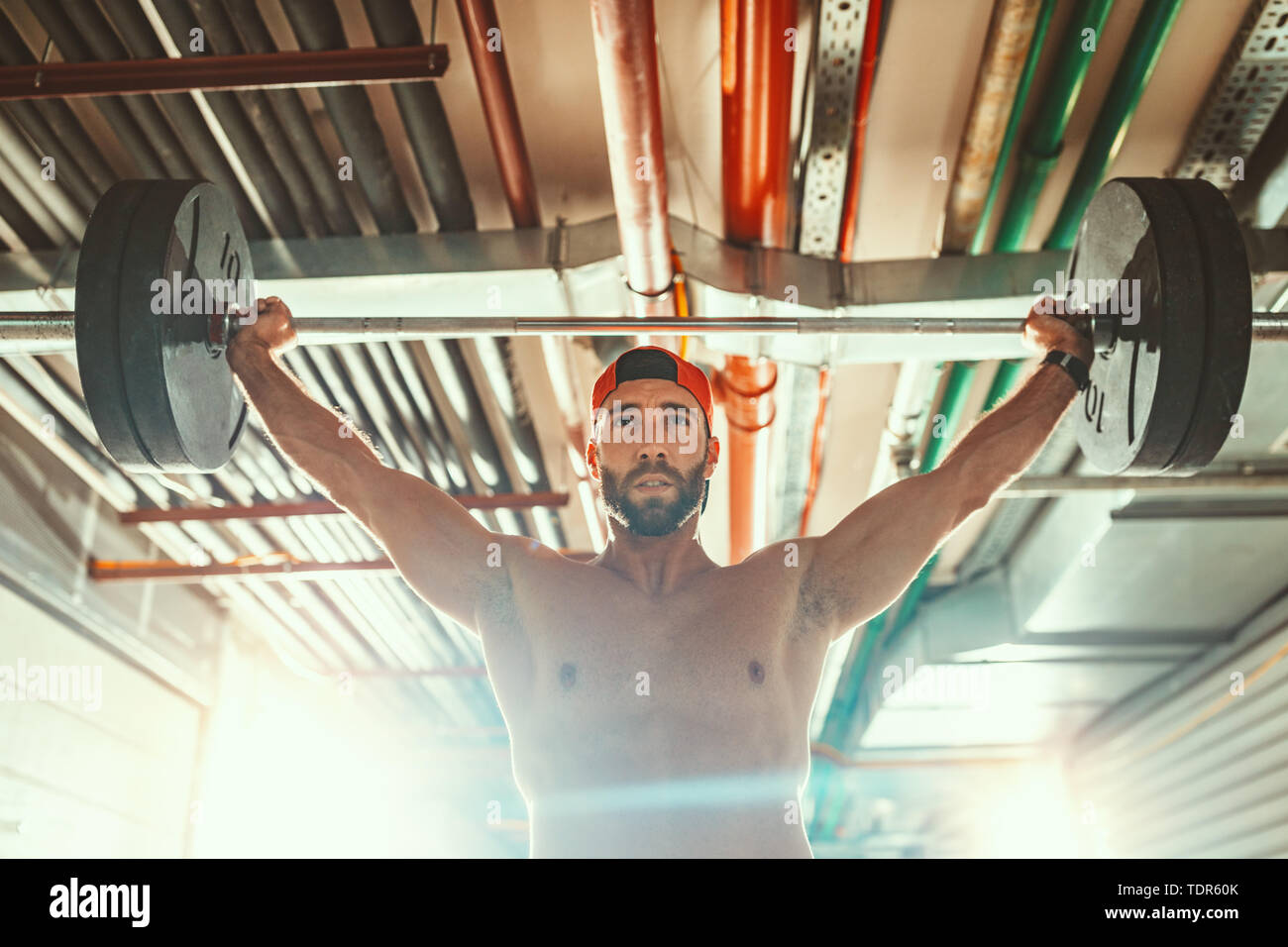 Young muscular man is doing snatch or shoulder press exercise with ...
