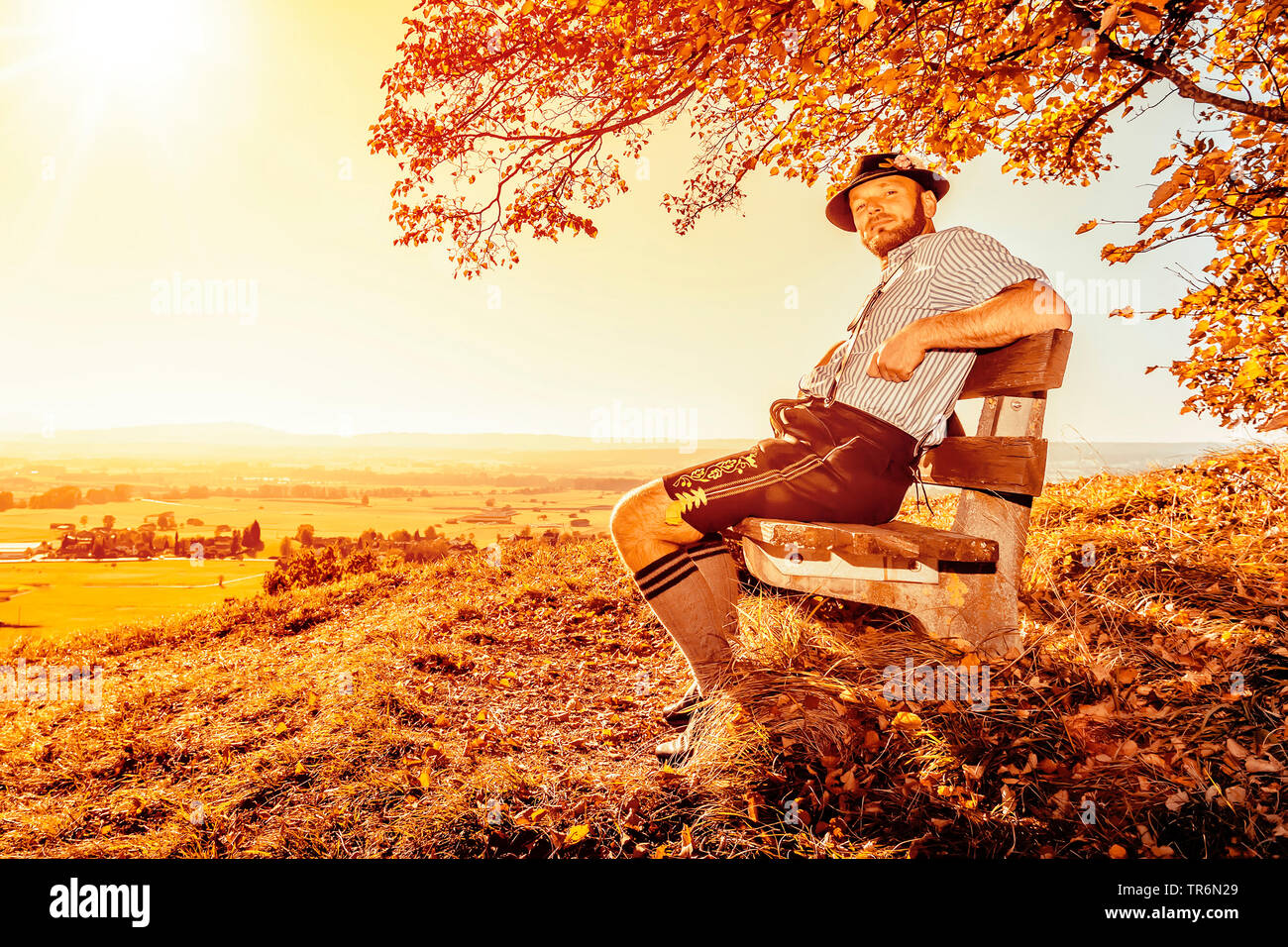 traditional clothed Bavarian man with Tyrolean hat sitting on a bench ...
